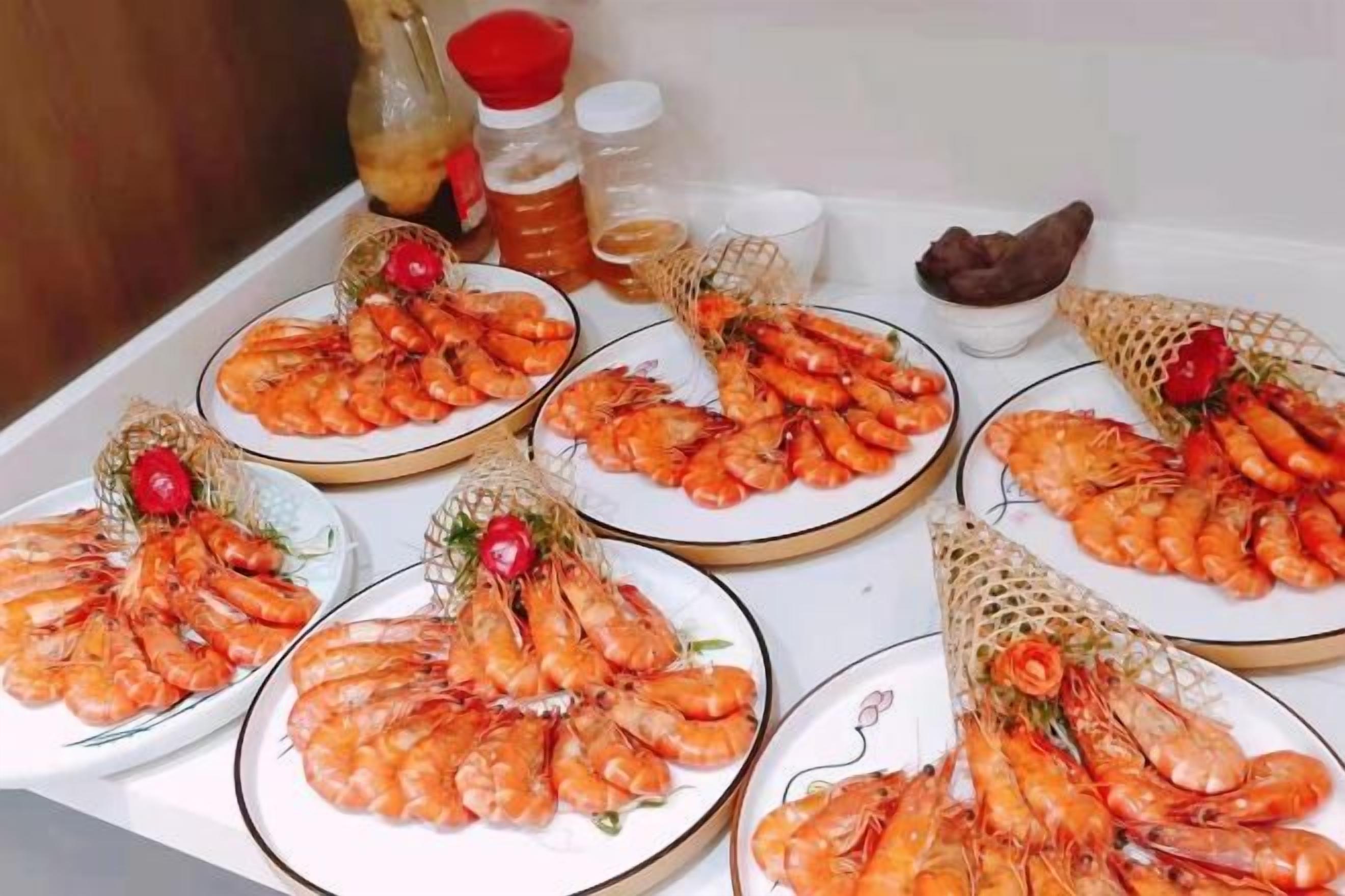 Mesa com pratos de camarão cozido, acompanhamentos e uma garrafa.