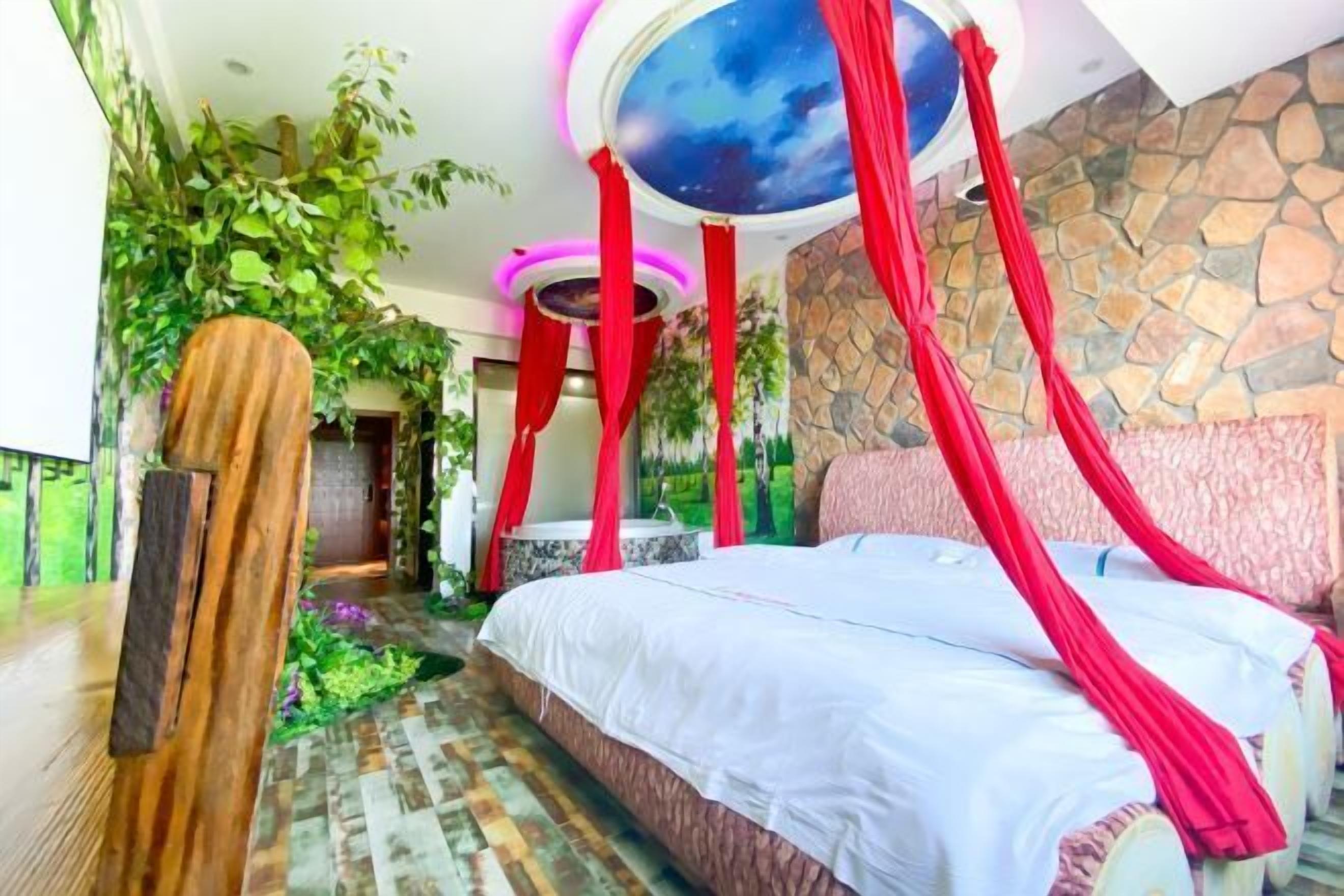 Quarto com cama, dossel vermelho, parede de pedra e vegetação.