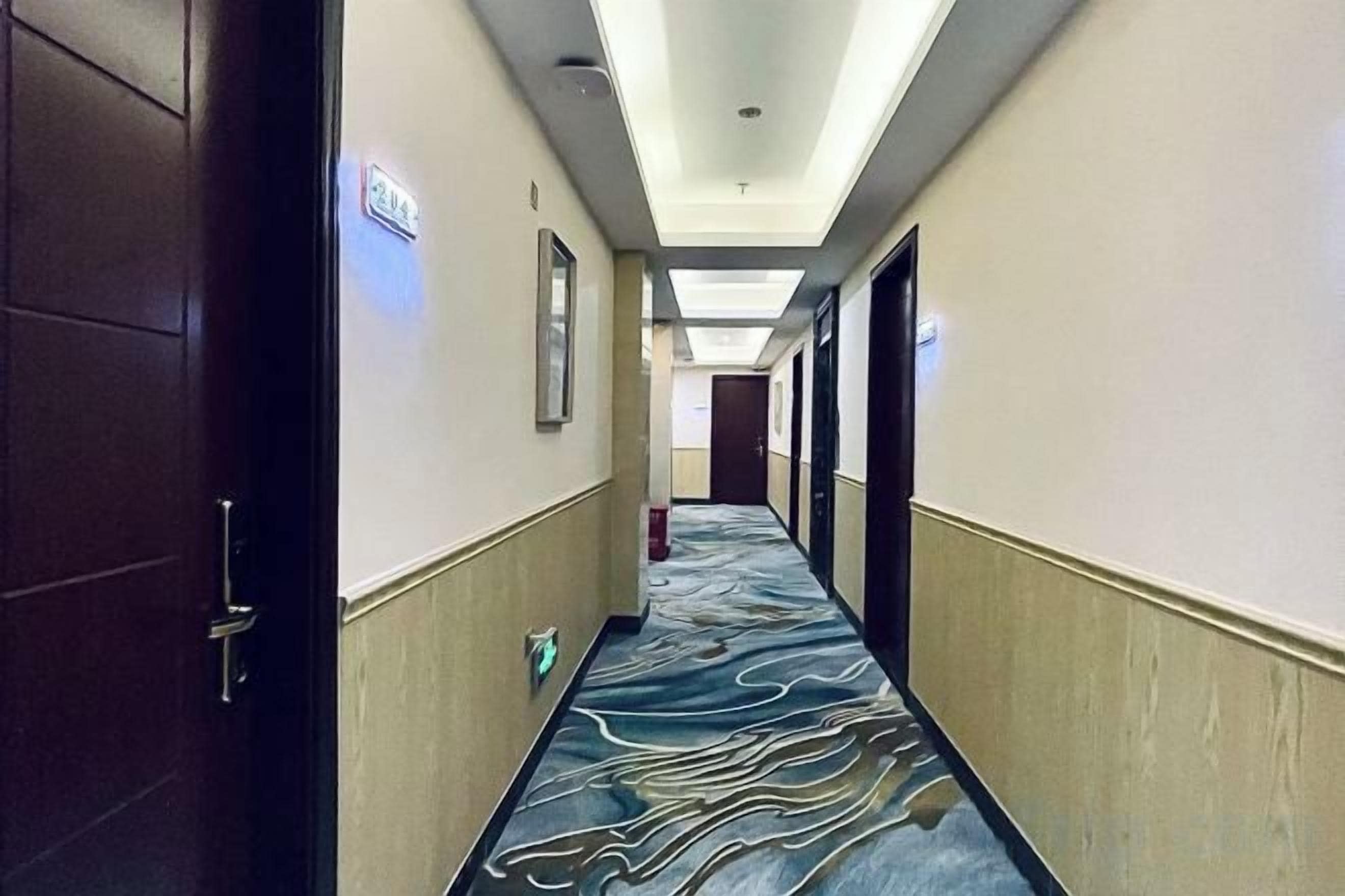 Corredor de hotel com carpete estampado, portas em ambos os lados e luminária no teto.