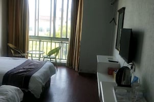 Quarto de hotel com cama, televisão, escrivaninha e cafeteira, além de varanda com cadeiras.