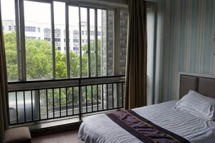 Quarto de hotel com uma janela ampla, uma cama e vista para edifícios e árvores.