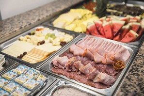 Buffet com diversos alimentos, incluindo carnes, queijos e frutas.