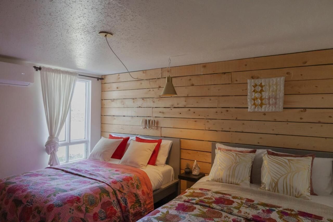 Quarto com duas camas, painéis de madeira nas paredes, janela com cortinas e luminária pendente.