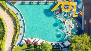 Vista aérea de uma área de piscina com escorregador, cercada por vegetação e um espaço de estar coberto.