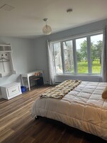 Quarto com cama grande, escrivaninha e cadeira. Janela com vista para o verde lá fora.