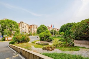 Área ajardinada com estrada, vegetação e edifícios residenciais ao fundo.