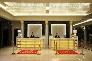 Uma área de recepção de hotel com dois balcões, um candelabro e um tapete vermelho.