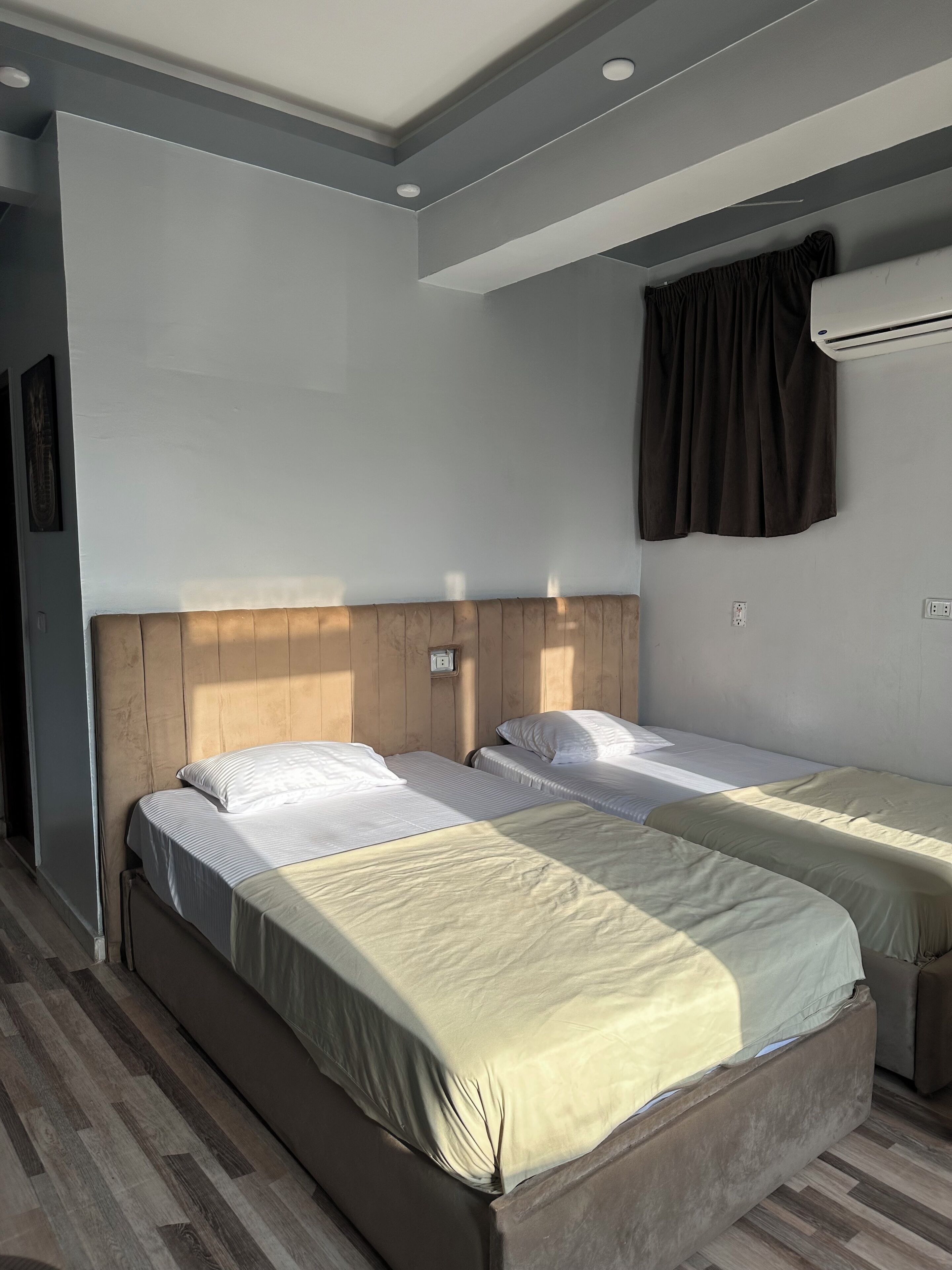Quarto com duas camas, cabeceira de madeira, ar-condicionado fixado na parede e tomada.