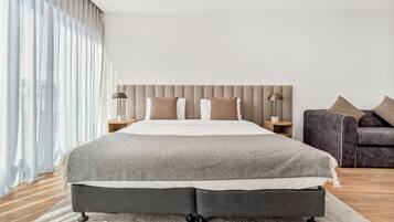 Quarto moderno com uma cama grande, um sofá estofado cinza e piso de madeira.