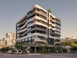 Um edifício de vários andares com fachada curva, varandas e um estacionamento com carros.