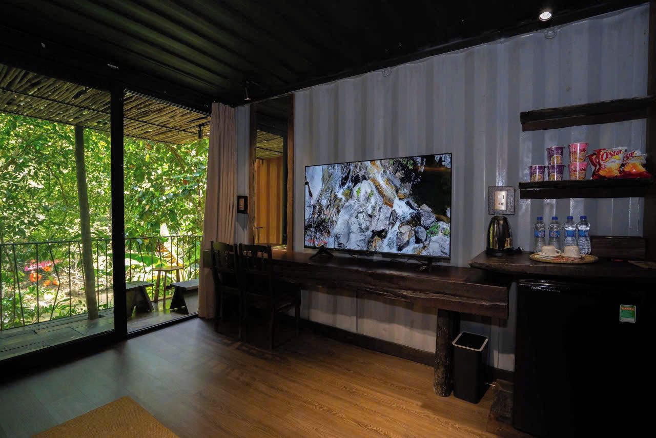 Sala de estar moderna com uma televisão de tela plana grande, móveis de madeira e vista para um verde exuberante pelas amplas janelas.