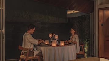 Um casal jantando à mesa com velas, uma taça de vinho e um menu.
