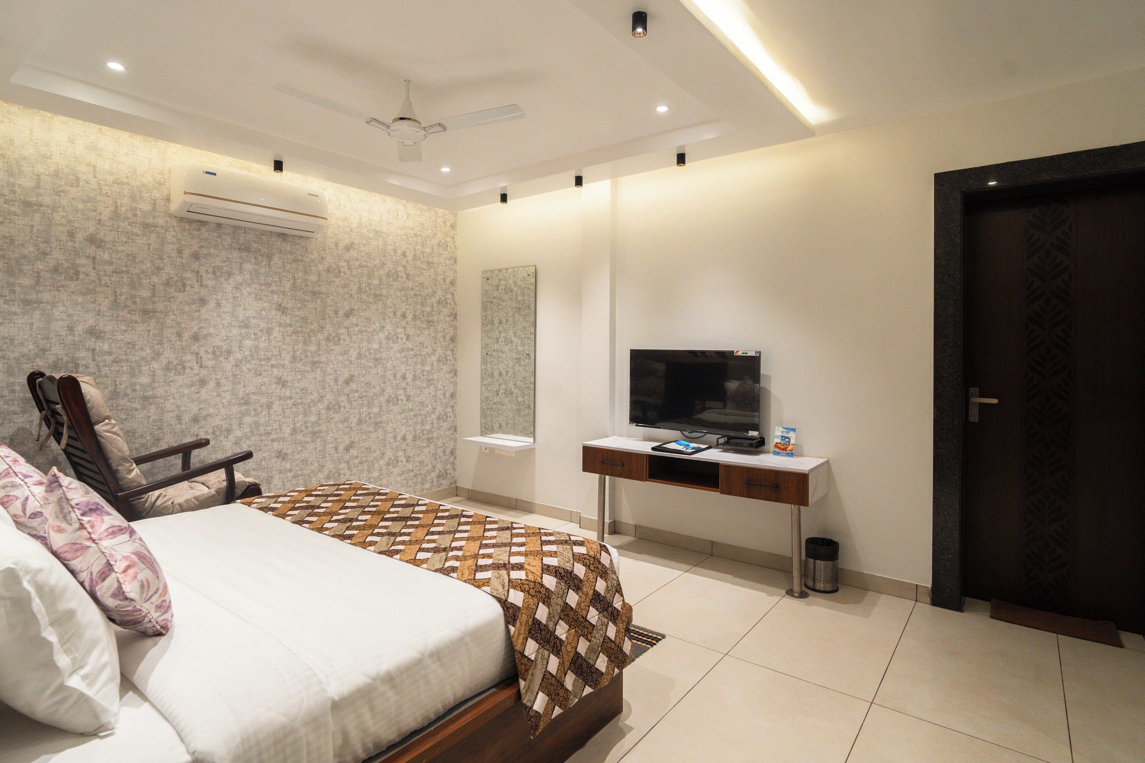 Quarto moderno com cama, escrivaninha, televisão e porta.