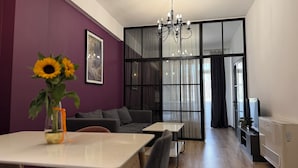 Uma sala de estar moderna com uma parede de destaque roxa, um candelabro, um sofá, uma mesa de jantar e uma janela grande com cortinas leves.