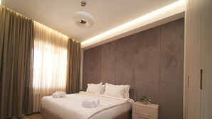 Quarto moderno com cama grande, piso de madeira, mesa de cabeceira com planta e luminária no teto.