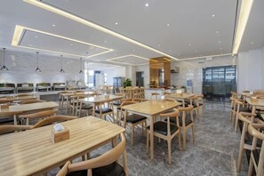 Uma sala de jantar moderna com mesas e cadeiras de madeira, piso de mármore e luminárias pendentes.