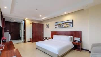 Quarto de hotel com uma cama grande, cabeceira de madeira, mesa de cabeceira, cadeira, escrivaninha e um quadro na parede.
