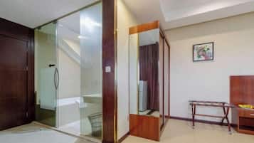 Quarto com porta de vidro deslizante para uma área de chuveiro, guarda-roupa de madeira, espelho e uma pequena mesa com cadeira.