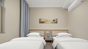 Quarto de hotel com duas camas, uma mesinha de cabeceira, uma obra de arte pendurada na parede e uma janela com cortinas.