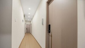 Um corredor com piso de madeira, paredes brancas e uma porta com puxador.