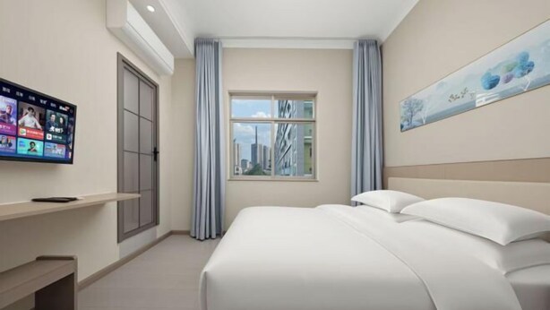 Quarto de hotel moderno com uma cama, televisão presa à parede, janela com vista para a cidade e um quadro na parede.
