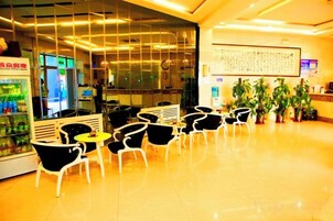 Um saguão de hotel com balcão de recepção, área de estar com cadeiras e máquina de venda automática.