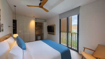 Quarto de hotel com cama, ventoinha no teto, televisão, varanda com vista e uma cadeira.