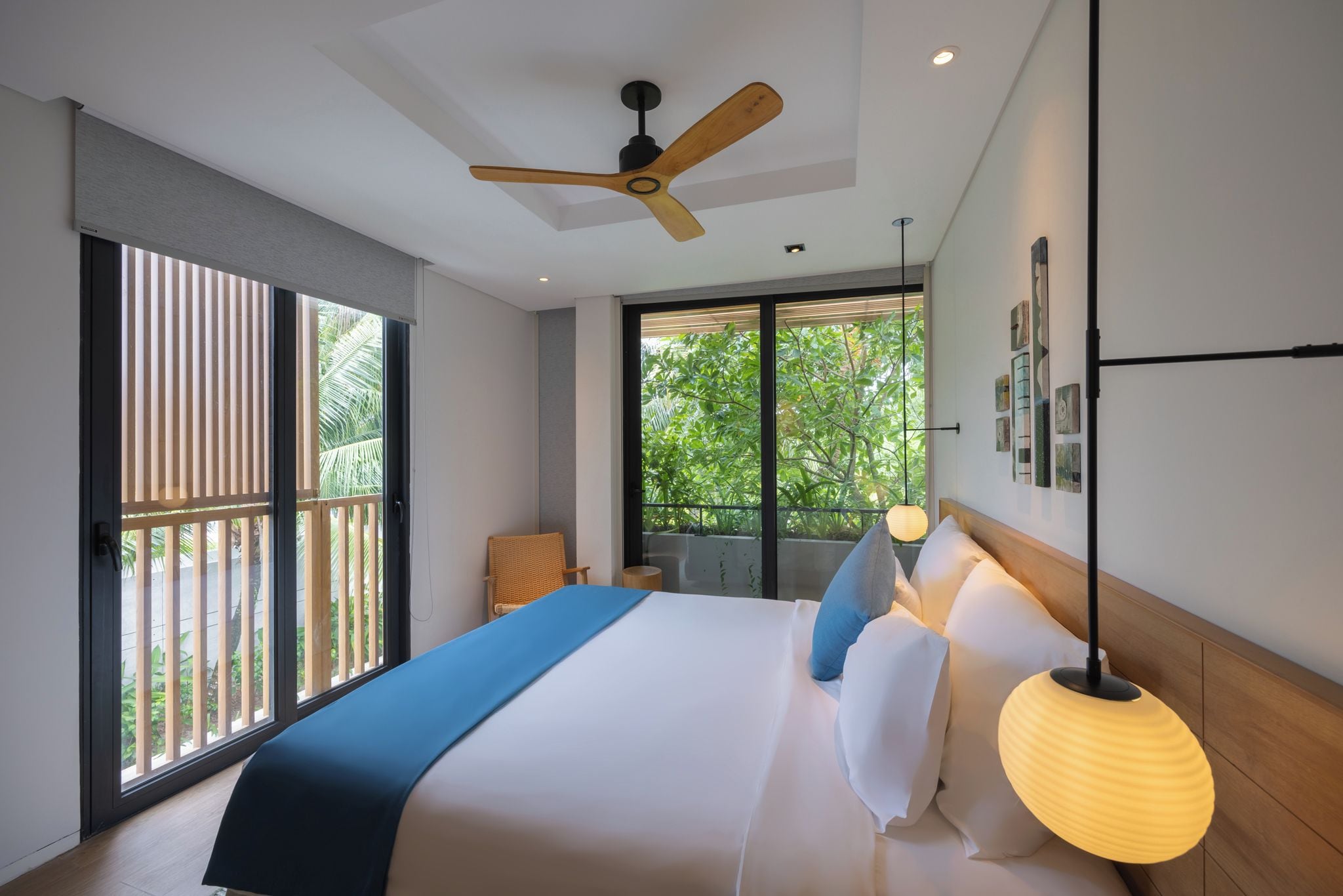 Quarto de hotel moderno com uma cama grande, um ventilador de teto e vista para o verde pelas janelas.