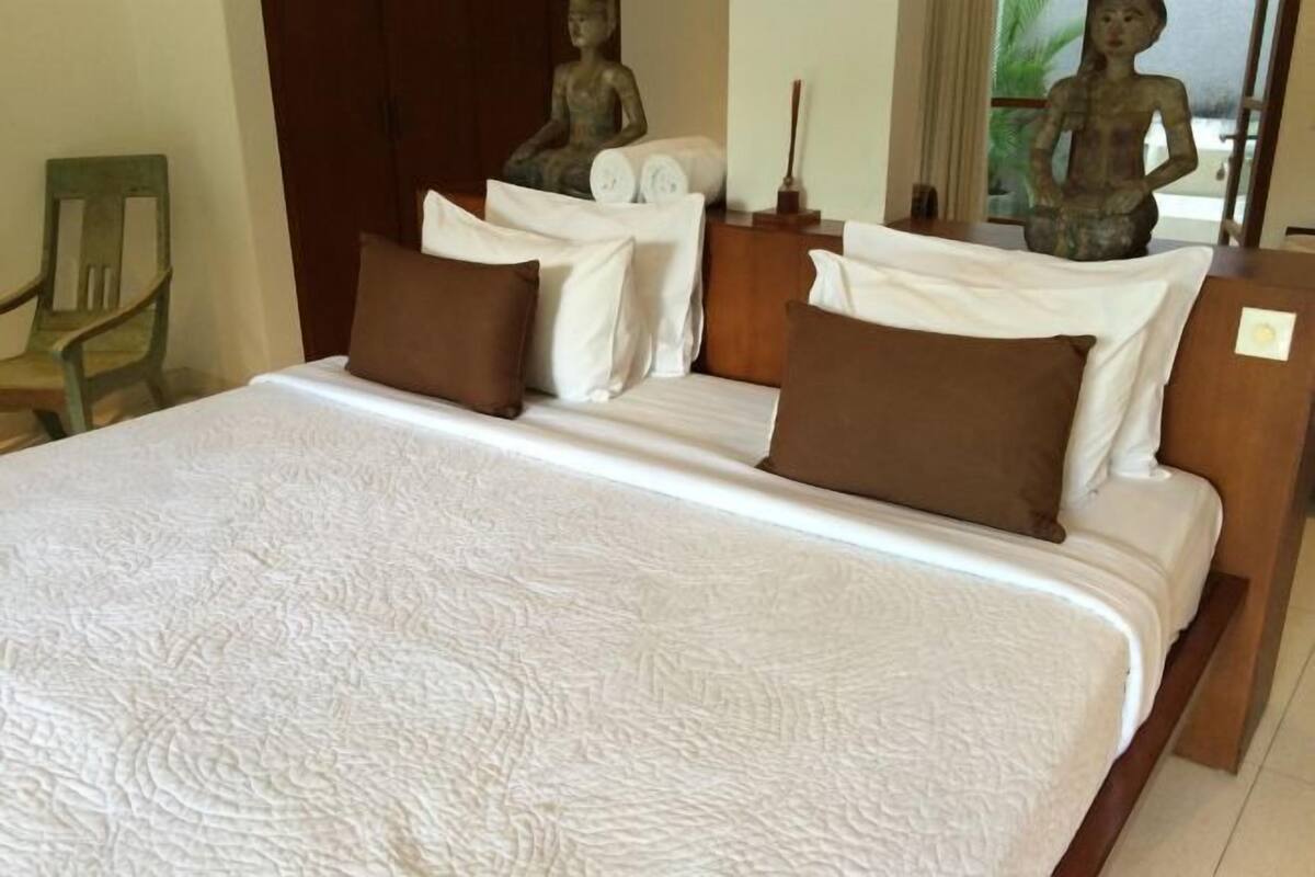 Uma cama com roupa de cama branca, almofadas castanhas e cabeceira de madeira.