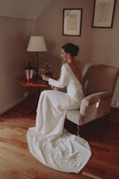 Quarto com piso de madeira, uma cadeira, uma mesa com abajur e um diploma emoldurado na parede.