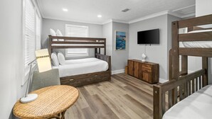 Um quarto com uma cama beliche, uma mesa de cabeceira com abajur, um pequeno armário e uma televisão na parede.