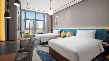 Quarto de hotel com duas camas, uma mesa de trabalho e vista para a paisagem urbana.