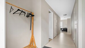 Um corredor com um suporte de madeira para roupas, um banco e uma porta que dá para uma sala de estar.