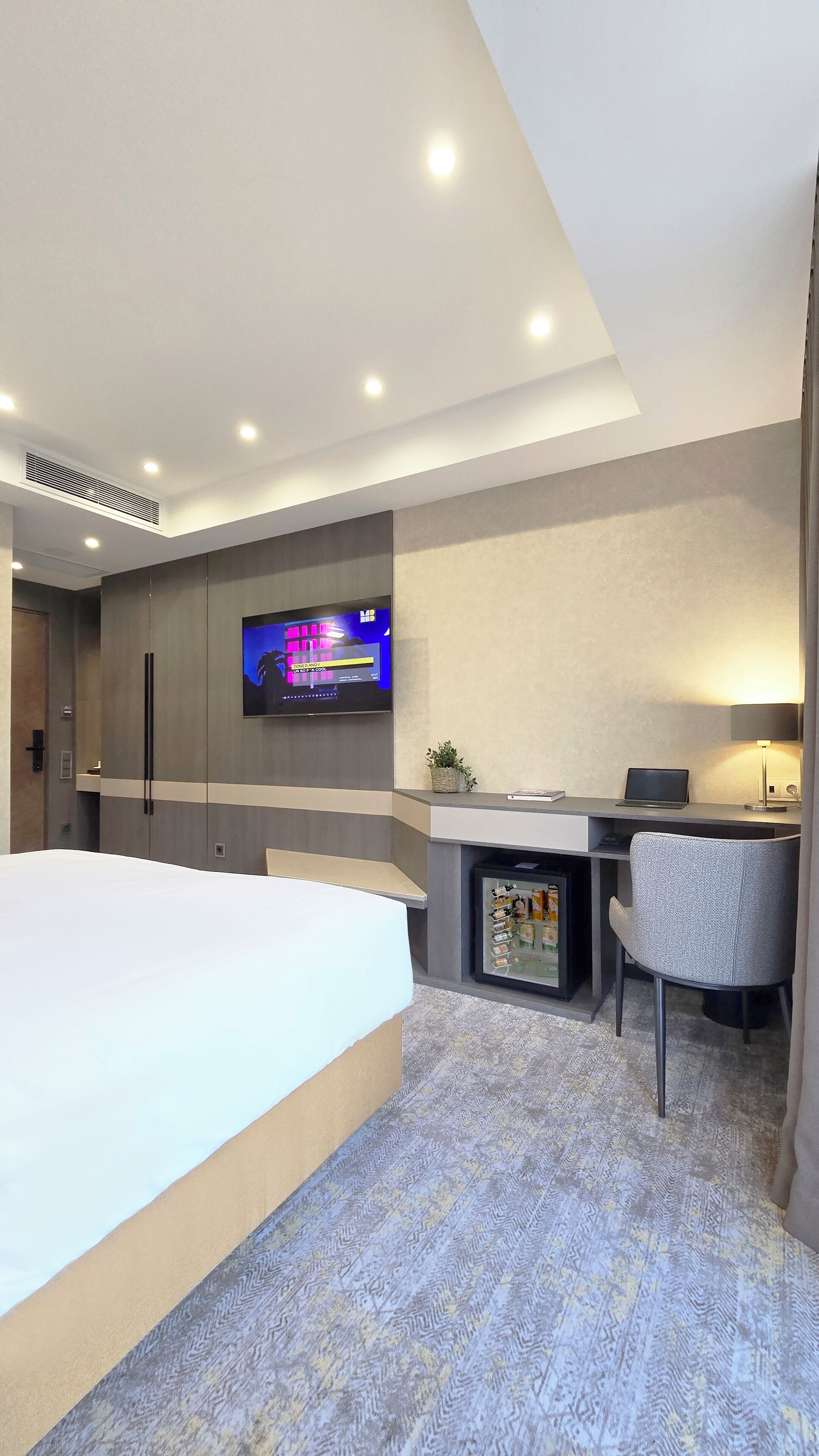 Quarto de hotel com cama, secretária com um laptop, televisão na parede e minibar.