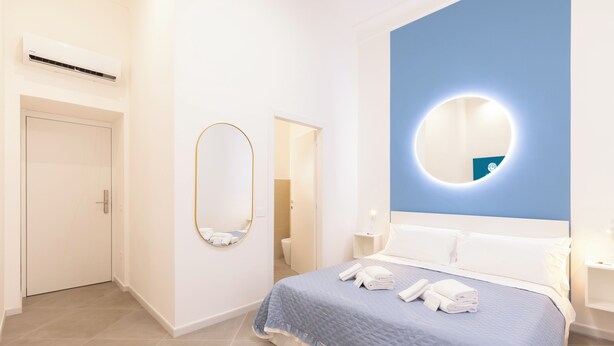 Quarto de hotel moderno com uma cama, um espelho redondo e uma parede azul de destaque.