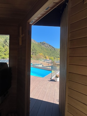 Um deck de madeira com piscina, vista para montanhas e céu claro.