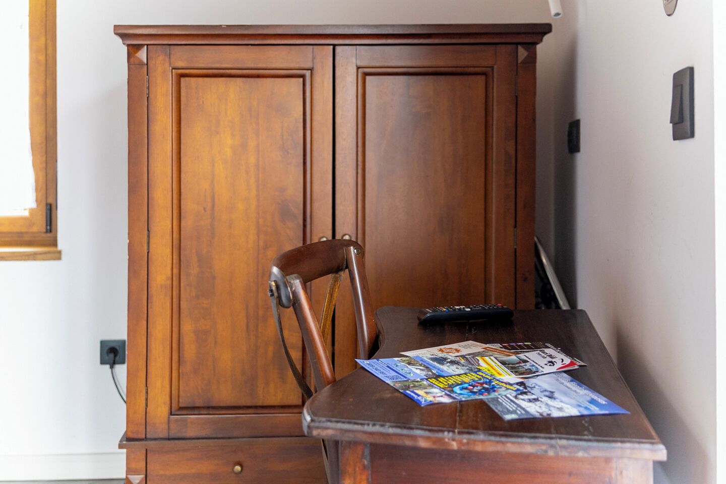Um armário de madeira com duas portas, uma cadeira e uma mesa com revistas.