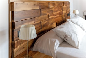 Uma cabeceira de madeira com design moderno, um abajur e uma cama bem arrumada com lençóis brancos e um travesseiro floral.