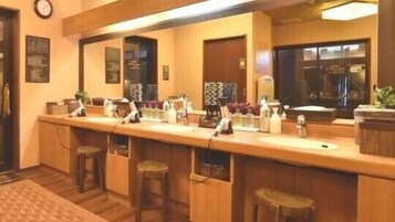 Casa de banho de hotel com bancada comprida, várias pias e banquetes.