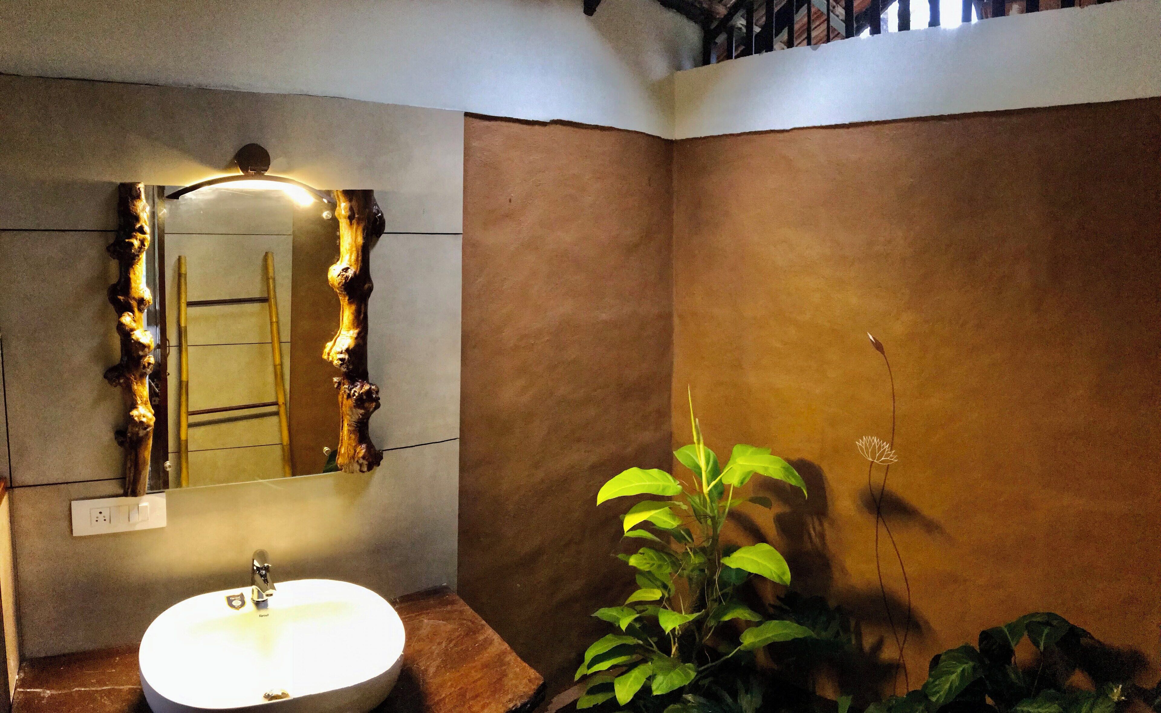 Uma casa de banho com uma pia redonda, um espelho com moldura de madeira e uma planta em vaso.