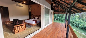 Quarto com cama e cadeira de madeira, e uma ampla porta de vidro deslizante que dá para uma varanda com piso de madeira.