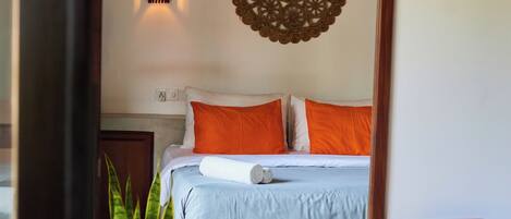 Quarto com cama, mesa de cabeceira, planta em vaso, cadeira de madeira e um objeto decorativo na parede.
