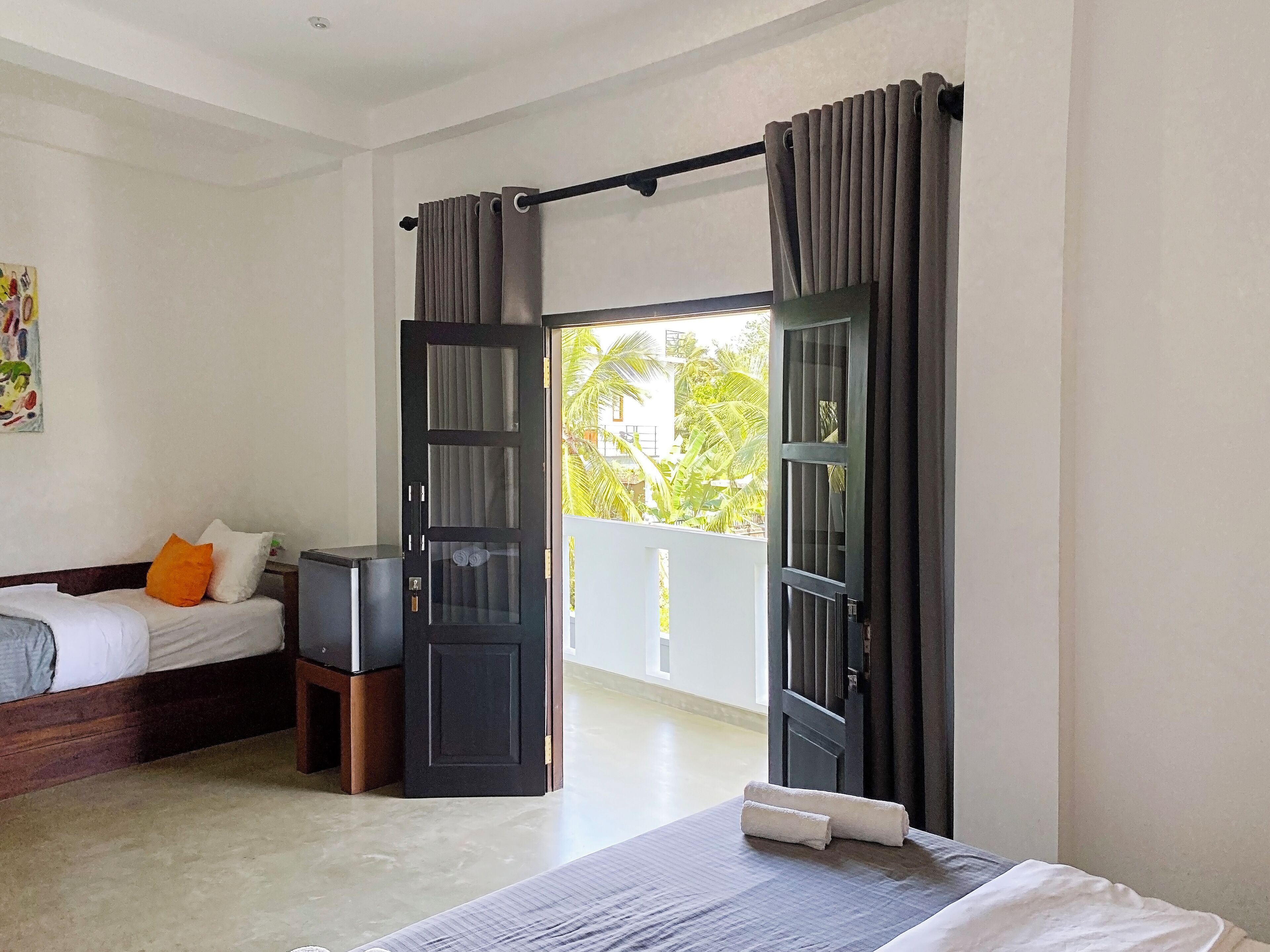 Quarto de hotel com cama, uma mesinha, televisão e varanda com cortinas.