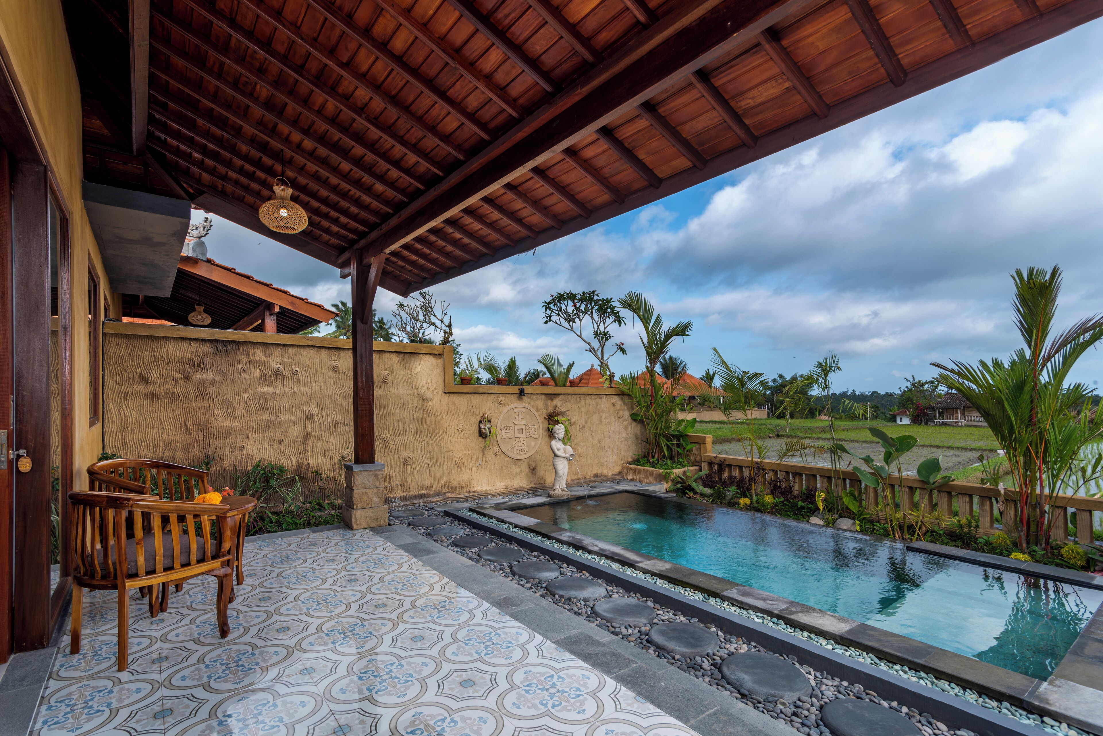 Uma área externa coberta com piscina, móveis de madeira e um painel decorativo.
