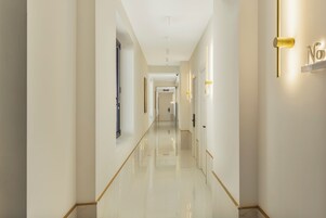 Um corredor moderno de hotel com piso brilhante, paredes brancas e detalhes dourados.