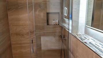 Uma casa de banho moderna com chuveiro em cabine de vidro, lavatório branco e um espelho grande.