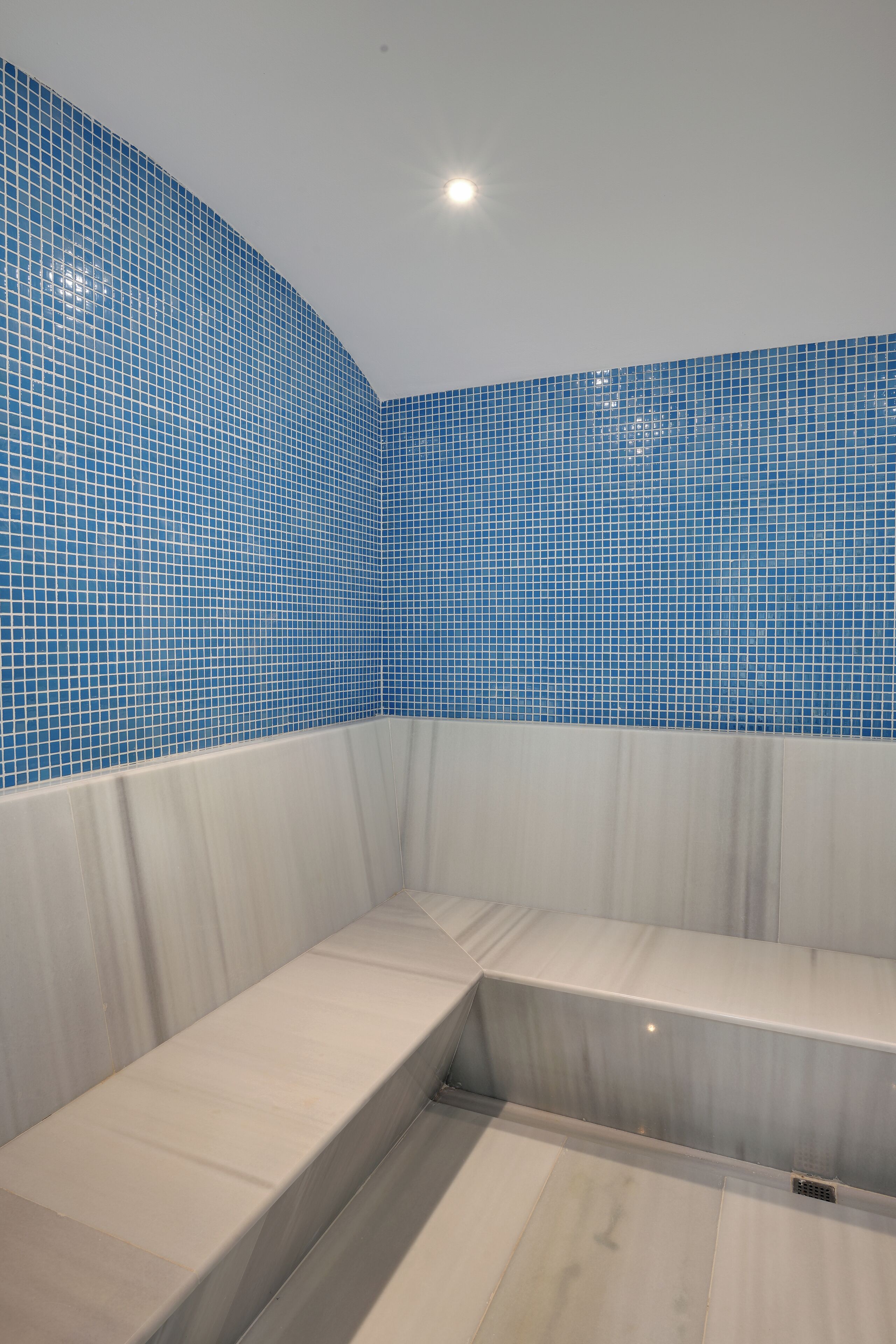 Canto de um quarto com um banco branco e parede revestida de azulejos azuis.