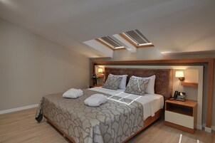 Quarto de hotel moderno com uma cama grande, claraboias, mesa de cabeceira com abajur e telefone.