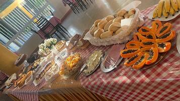 Mesa de buffet com diversos alimentos, incluindo pão, doces e frutas.