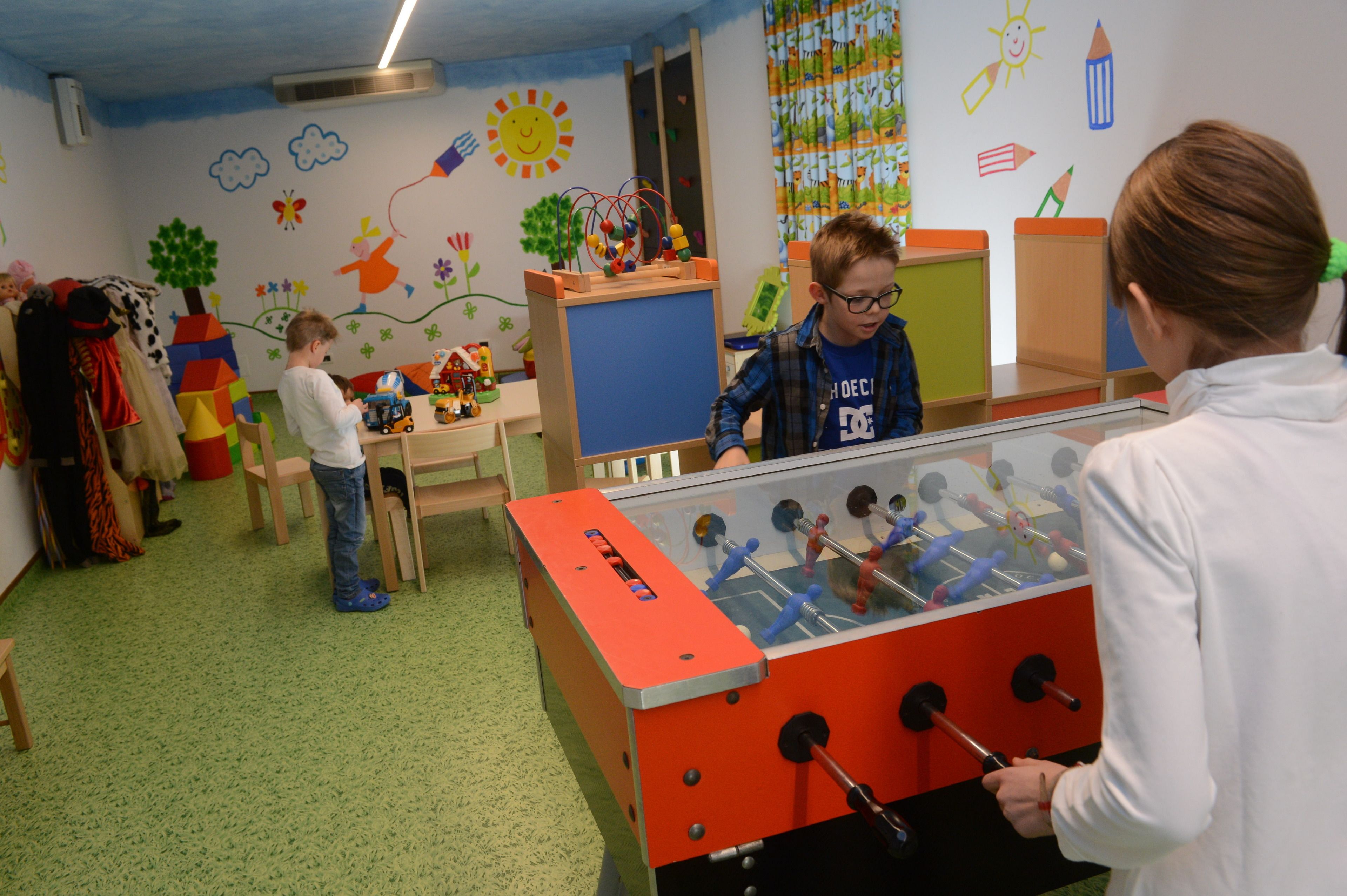 Uma sala de jogos infantil com mesa de pebolim, brinquedos e decorações educativas nas paredes.